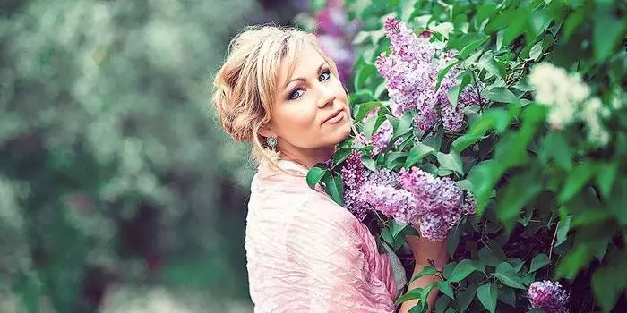 在盛開的淡紫色灌木旁邊的女人