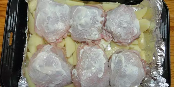 Muslos de pollo en una almohadilla de papa antes de hornear en una bandeja para hornear