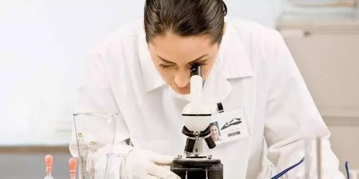 Ayudante de laboratorio mirando a través de un microscopio