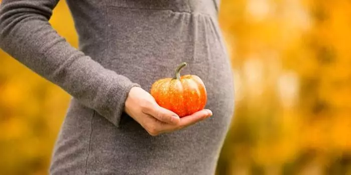 Una mujer embarazada sosteniendo una calabaza.