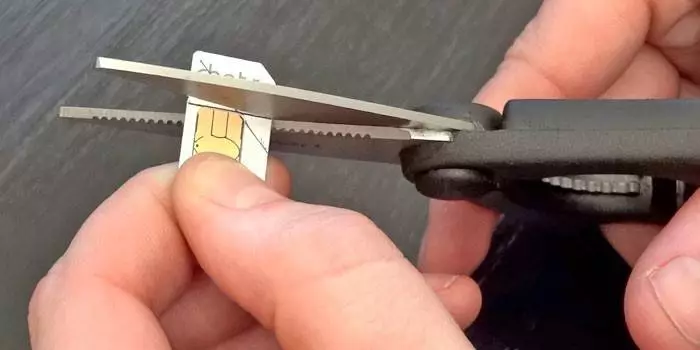 一个男人根据模板用剪刀剪一张 SIM 卡