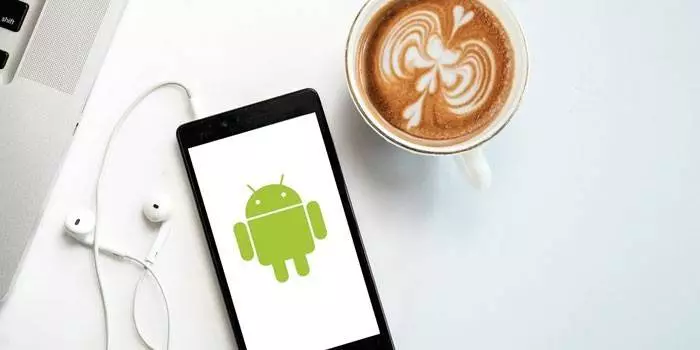 Smartphone con auriculares e unha cunca de café