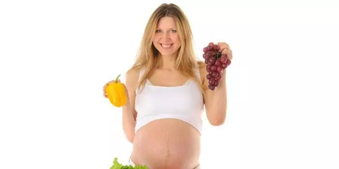 Těhotná žena držící v rukou papriky a hrozen