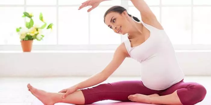 Těhotná žena provádějící cvičení, zatímco sedí na podlaze