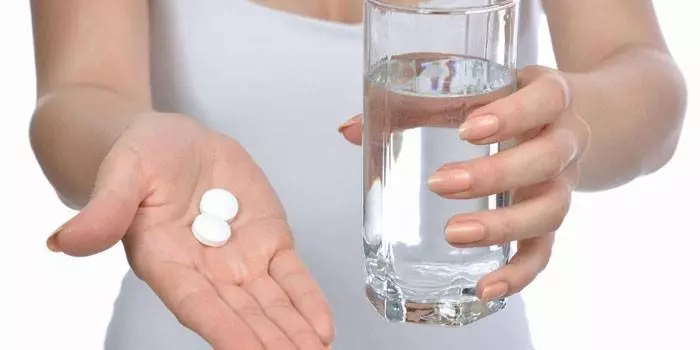 Pilulky a pohár vody v rukách dievčaťa