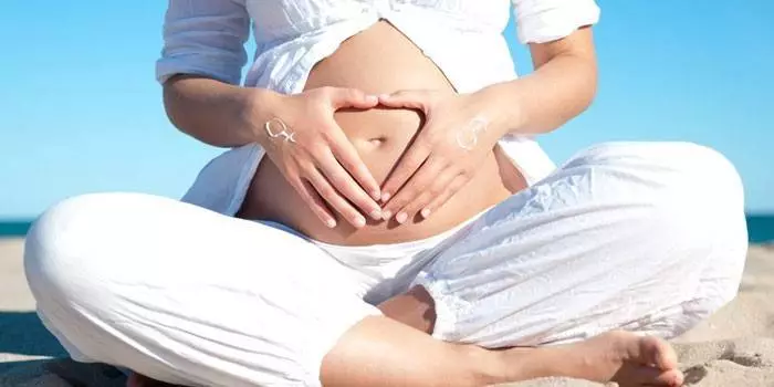 Έγκυος κοπέλα που κάθεται σε στάση λωτού στην άμμο