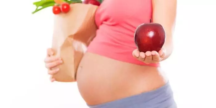 हाथ की हथेली में सेब पकड़े गर्भवती लड़की