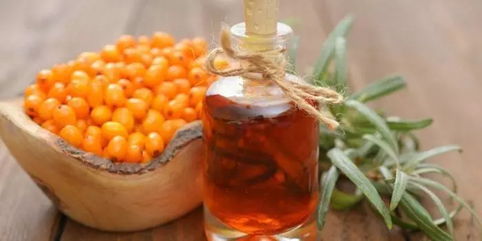 Minyak buckthorn segara ing botol lan woh-wohan buckthorn segara ing piring