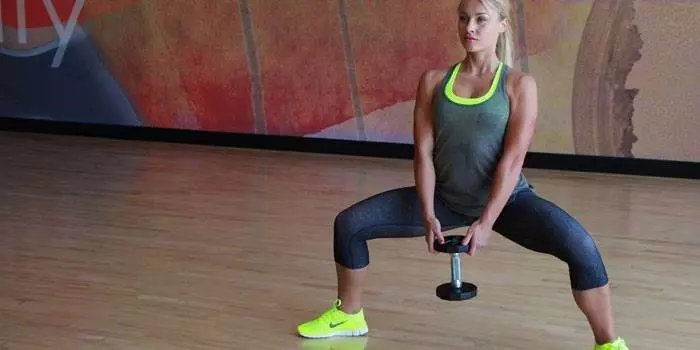 Girl doing sumo squat with a dumbbell between her legs