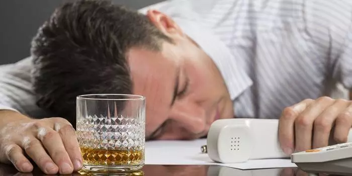 Muž spí pri stole s pohárom a telefónnym prijímačom