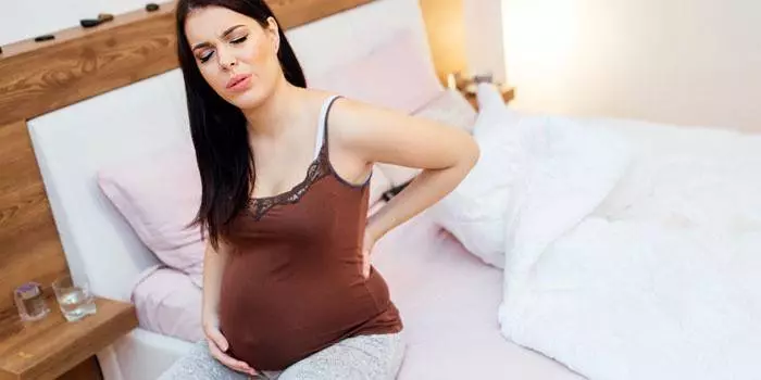Těhotná žena sedí na posteli