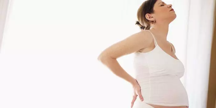 Una dona embarassada sosté la part baixa de l’esquena amb les mans