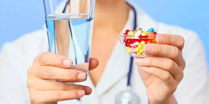 Pastillas y un vaso de agua en manos de un médico.