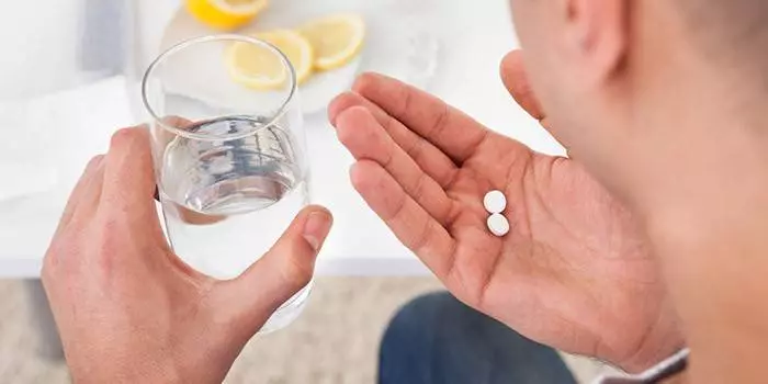 A man holds two pills and a glass of water in his hands