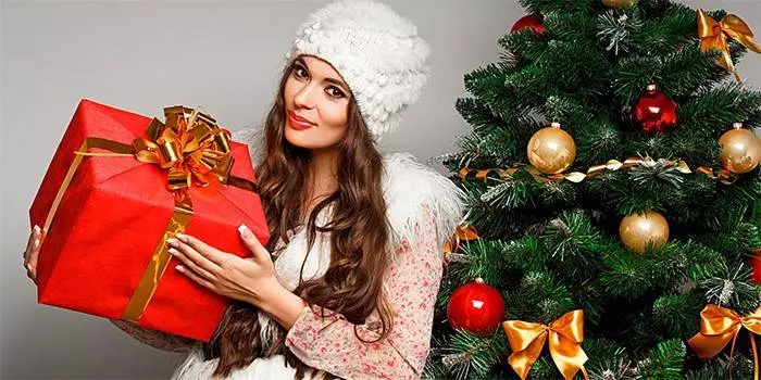 دختری در کنار درخت کریسمس با هدیه