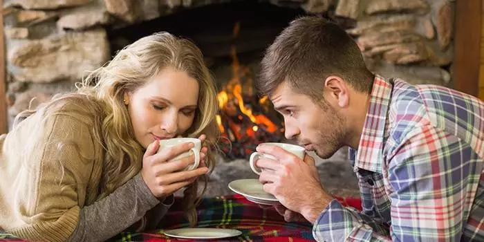 Laki-laki dan perempuan sedang minum teh di dekat perapian