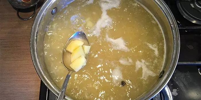 Chicken broth in a saucepan and potatoes in a spoon