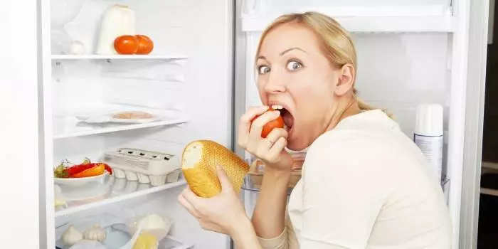 Mujer comiendo junto al frigorífico