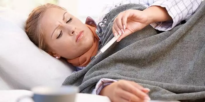 Uma mulher está deitada na cama e olha para um termômetro