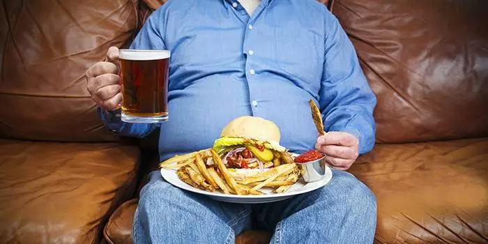 A man sitting on a sofa with a glass of beer and a plate of fast food