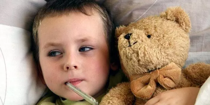 Dječak leži u krevetu s termometrom u ustima