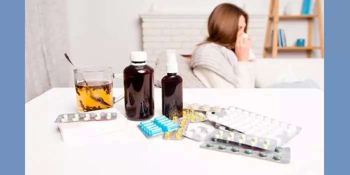 Žena sa prehladom i lijekovima na stolu
