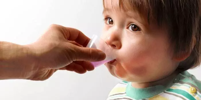 Al niño se le da jarabe de una taza medidora.