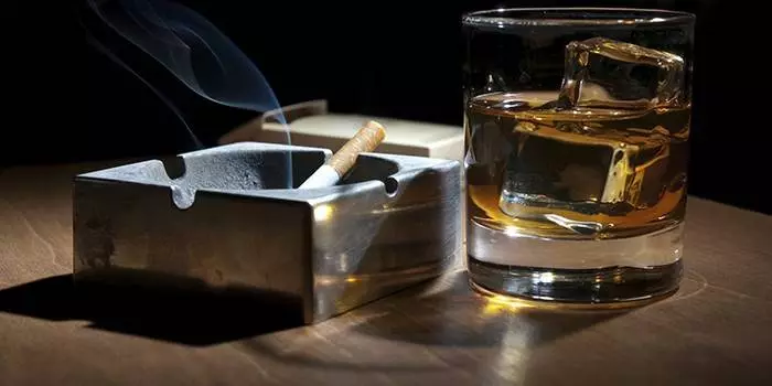 Sigaret in een asbak en een glas met alcohol en ijs