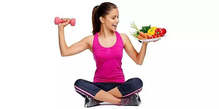 Girl holding dumbbells and a plate of vegetables in her hands