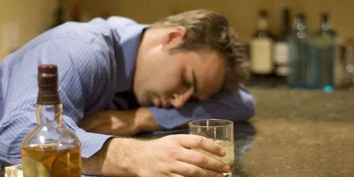 Vīrietis guļ uz galda ar alkohola glāzi rokā