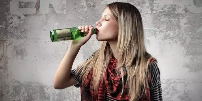 La ragazza beve birra da una bottiglia