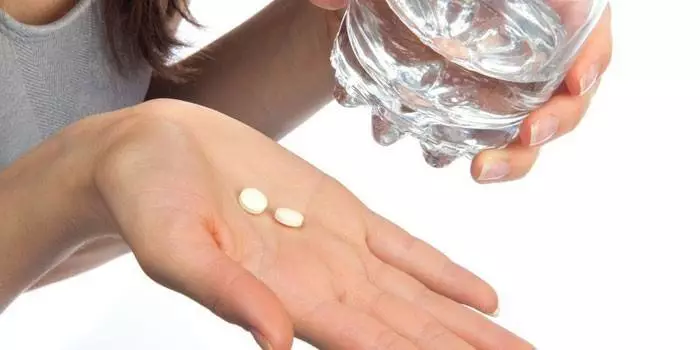 Tabletes ant delno ir stiklinę vandens