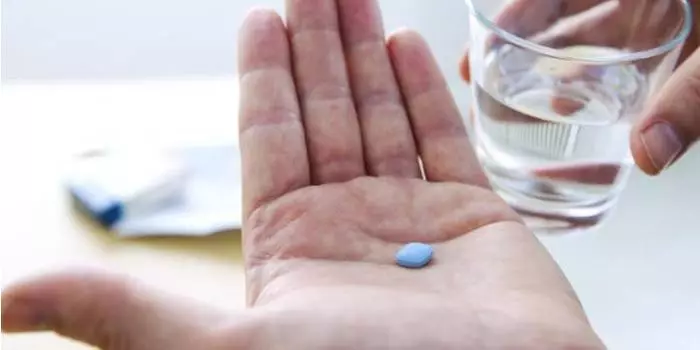 Medicina en la palma y un vaso de agua.