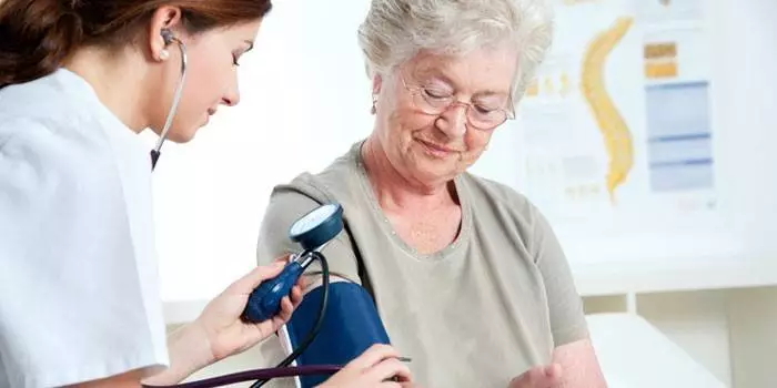 Bir doktor yaşlı bir kadında kan basıncını ölçer.