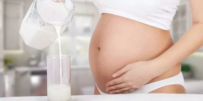 Gruaja shtatzënë derdh qumësht të pjekur të fermentuar në një gotë