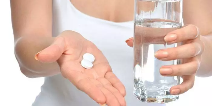 Tablete na dlanu i čaša vode u ruci