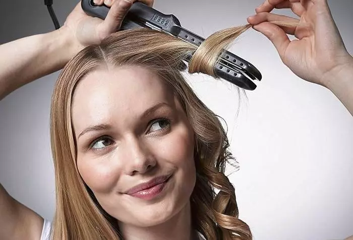 La fille fait des boucles avec un fer à repasser